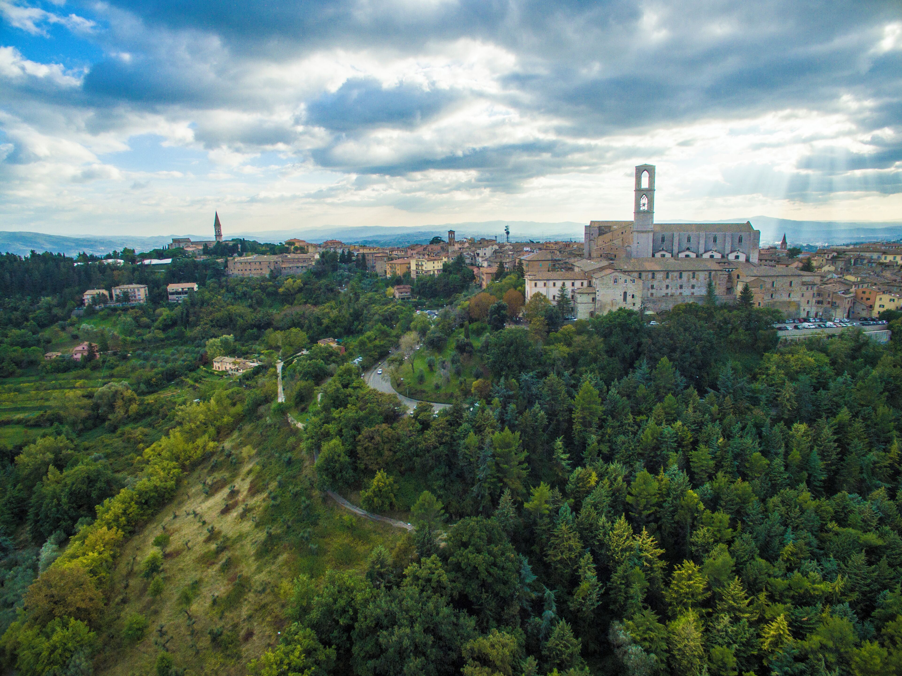 Uma cidade histórica com uma igreja imponente, destacando-se uma alta torre do sino, cercada por vegetação exuberante e uma estrada sinuosa.
