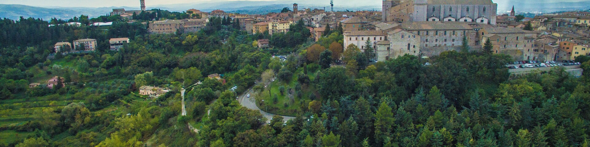 Uma cidade histórica com uma igreja imponente, destacando-se uma alta torre do sino, cercada por vegetação exuberante e uma estrada sinuosa.