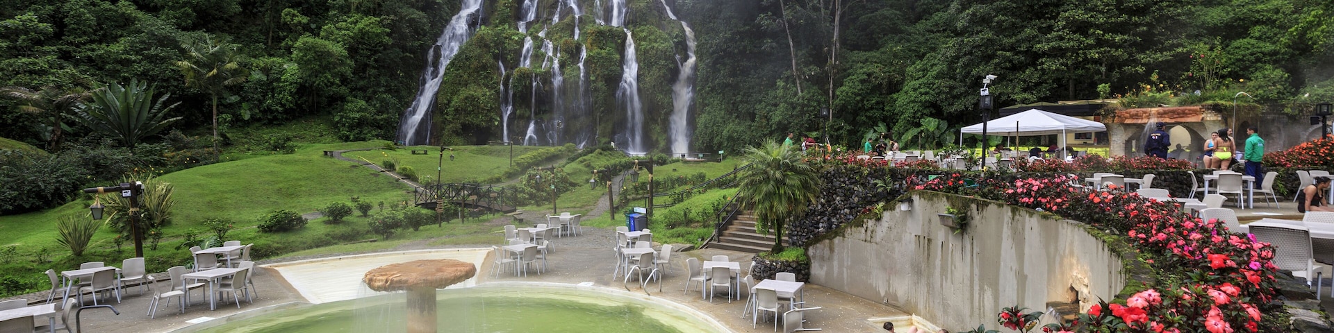 Uma cascata rodeada por vegetação exuberante e um jardim com flores cor-de-rosa.