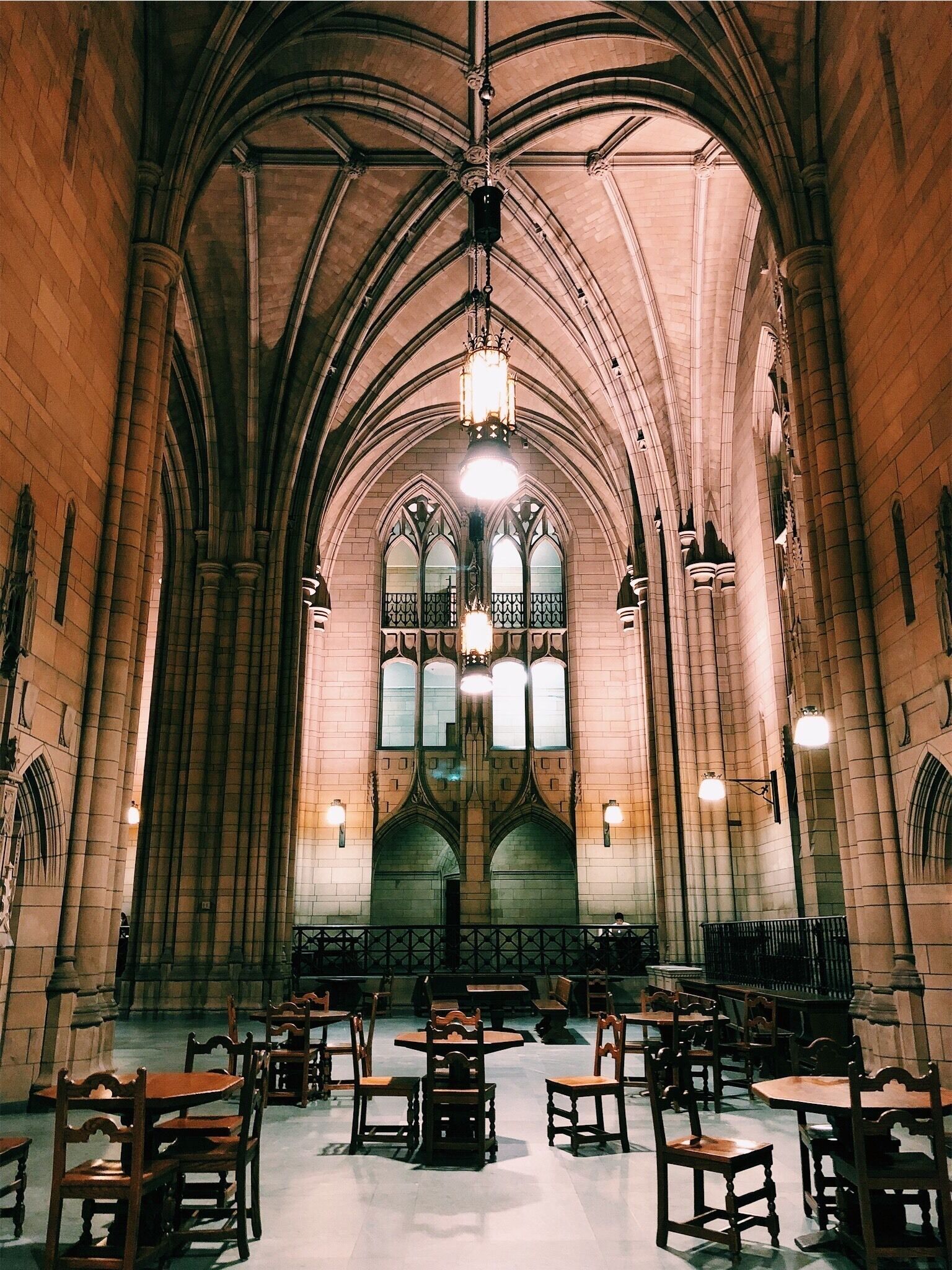 Interior de uma catedral com altos tetos abobadados, grandes vitrais e fileiras de bancos de madeira.
