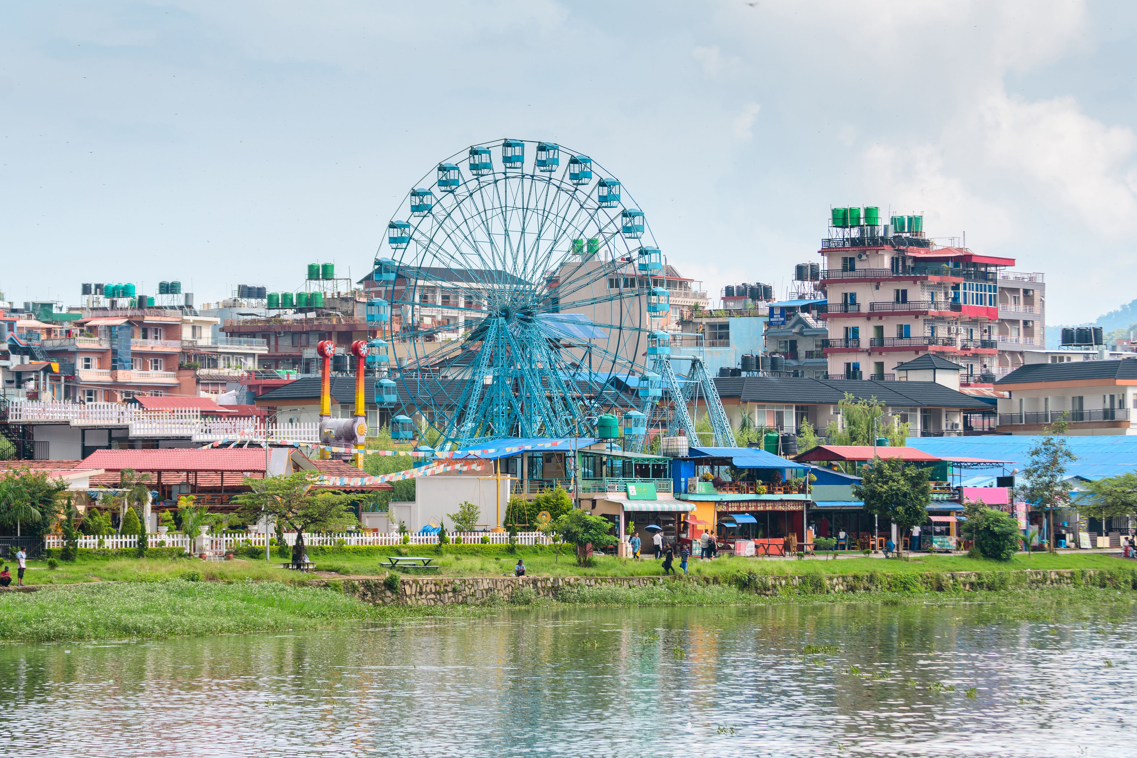 Uma grande roda gigante, um corpo d'água e uma área urbana densamente construída com diversos edifícios.