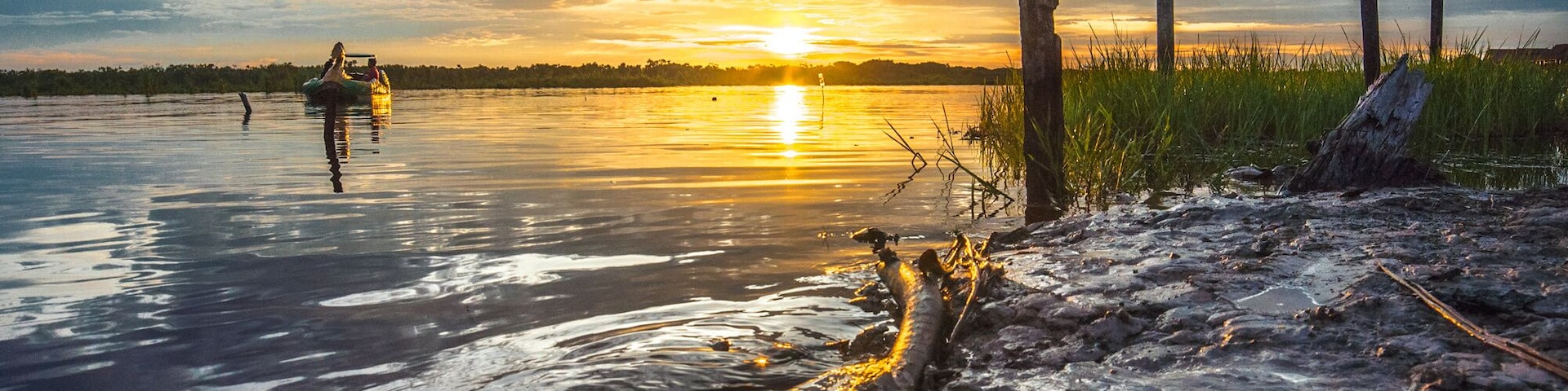 Um pôr do sol sobre um lago calmo, com uma cerca de madeira e um tronco na margem.