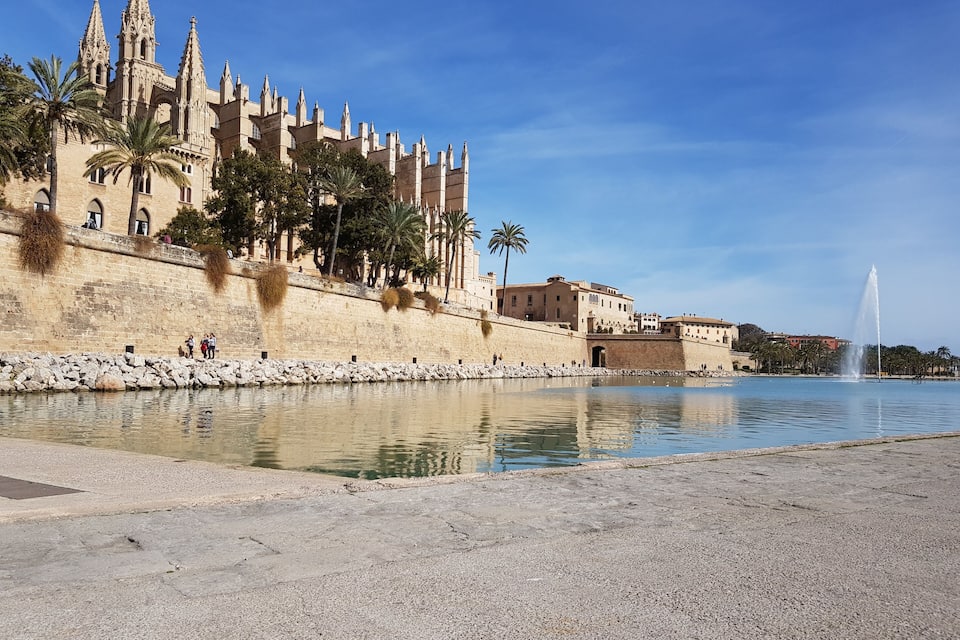 Um edifício histórico com arquitetura gótica, uma orla tranquila e uma fonte.