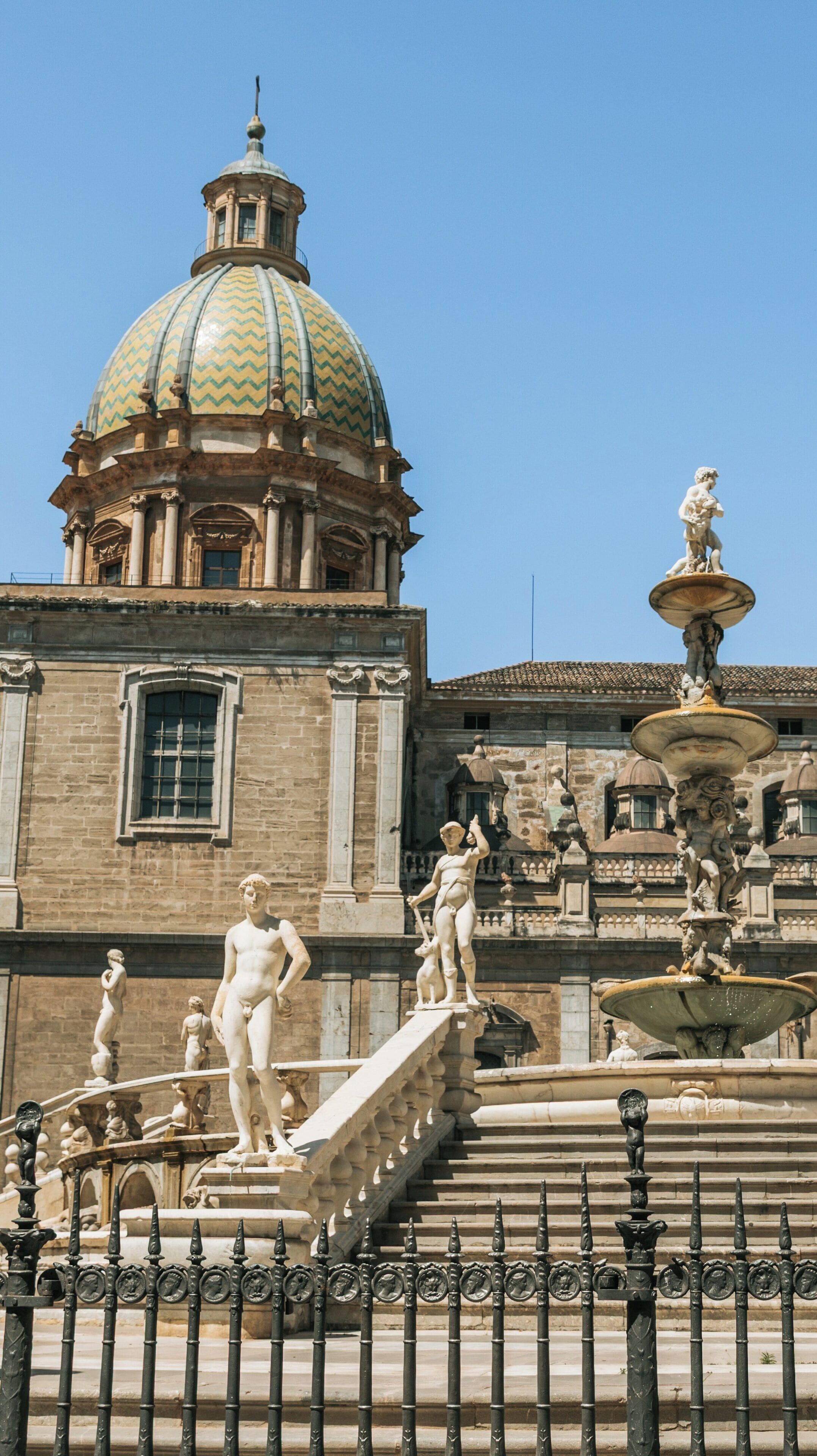 Stunning Pretoria Fountain showcases intricate sculptures against the backdrop of Kalsa neighborhood in Palermo, Sicily, Italy under clear blue skies