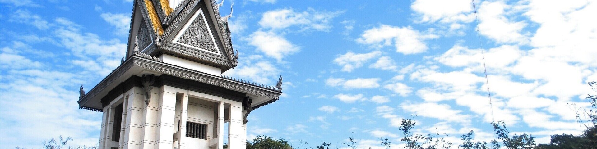 Um templo tradicional com telhado pontiagudo e decorações elaboradas, rodeado por um jardim bem cuidado e árvores.