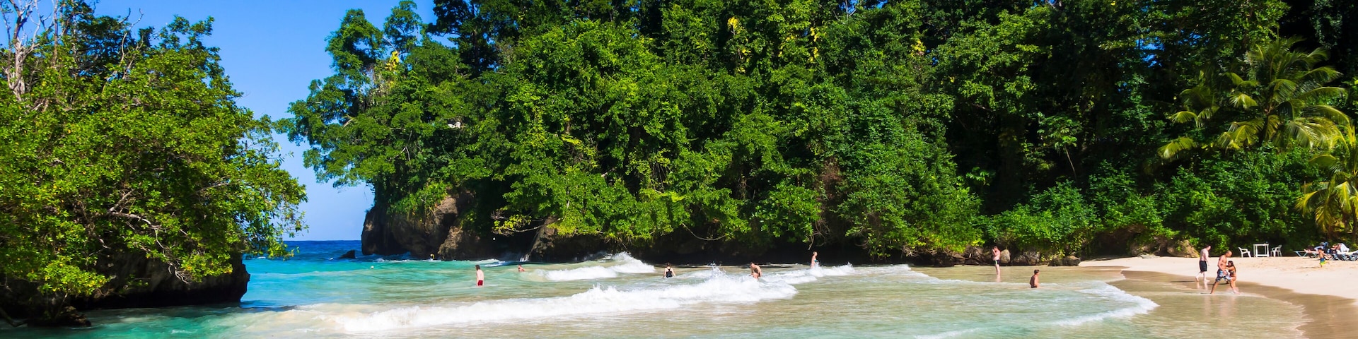 Uma praia com águas turquesa cristalinas, areal arenoso e vegetação verde exuberante.