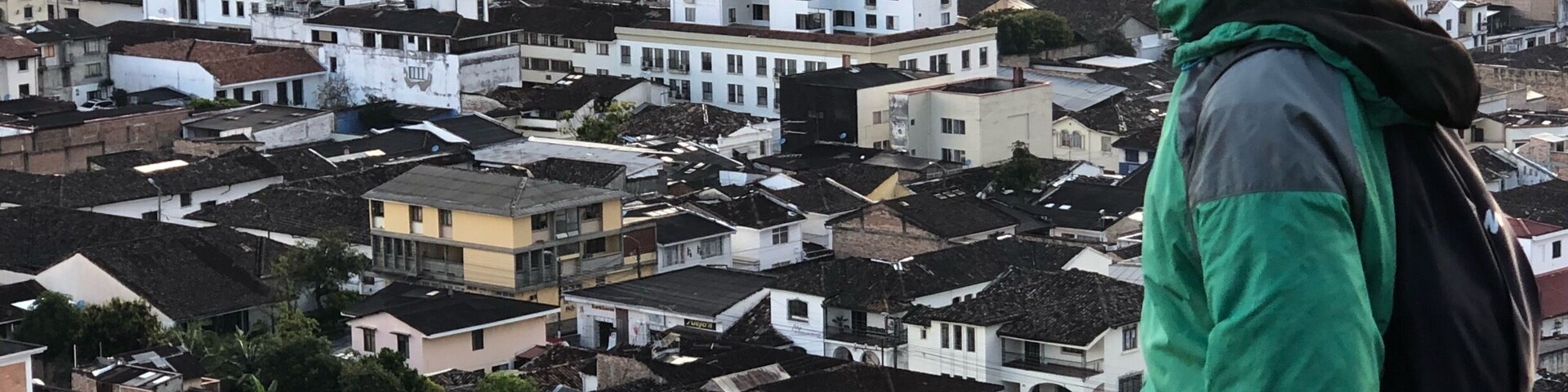 Uma pessoa observa uma área urbana densamente povoada, com mistura de edifícios tradicionais e modernos, incluindo uma estrutura abobadada branca proeminente ao longe.