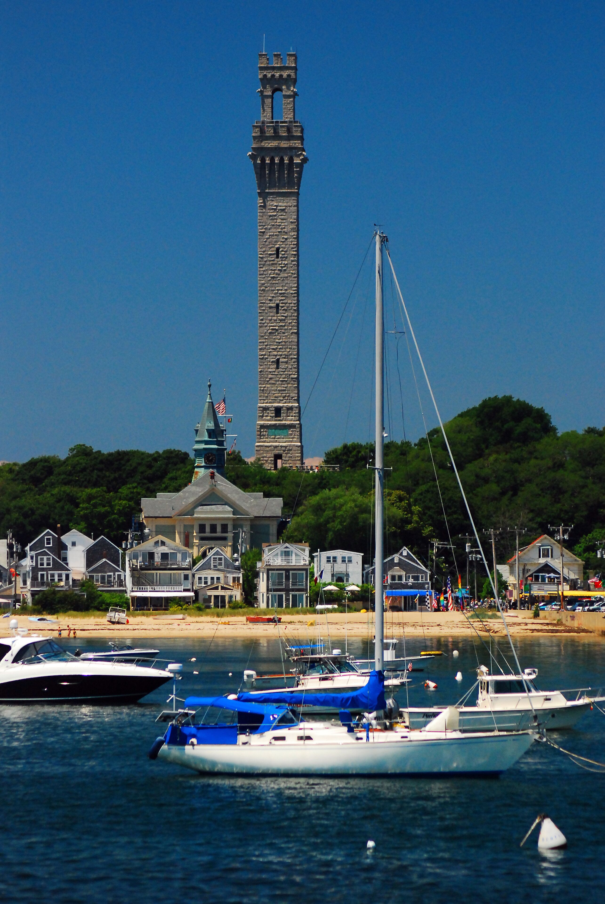 Uma vila costeira com uma torre imponente, alguns barcos e casas ao longo da praia.