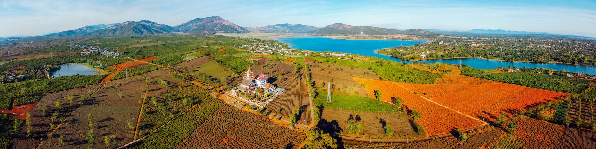 Vista aérea de uma paisagem com campos em socalcos, uma grande massa de água e montanhas ao longe.