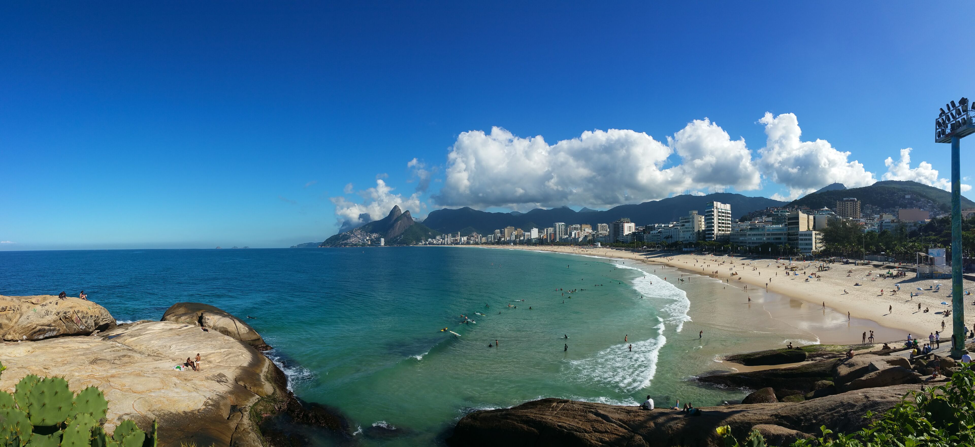 Paisagem costeira com praia, águas azul-claras e uma cordilheira ao fundo.