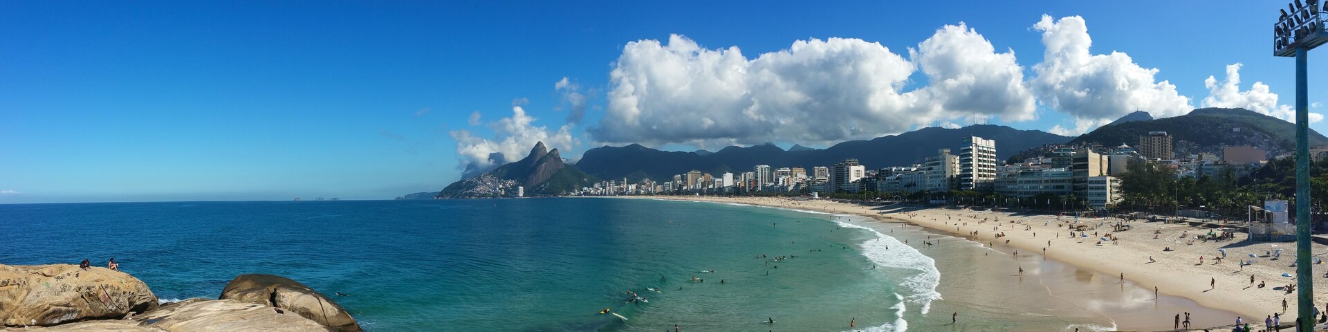 Paisagem costeira com praia, águas azul-claras e uma cordilheira ao fundo.