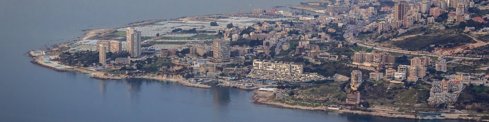 Paisagem costeira urbana densa, com um navio em destaque ao longe e um litoral curvo.