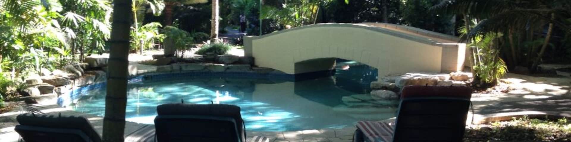 Piscina rodeada por vegetação exuberante e uma ponte de pedra.