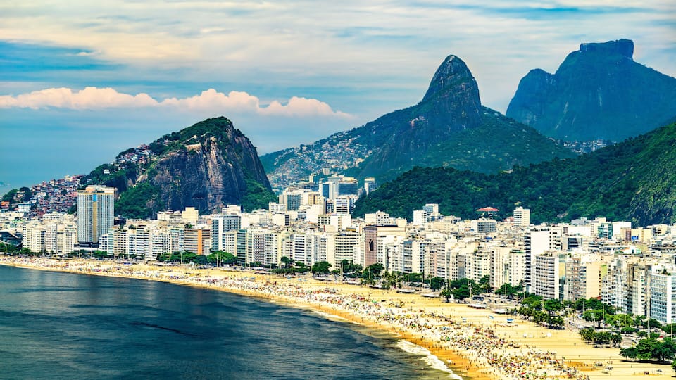 Paisagem costeira com uma montanha imponente e uma praia movimentada.