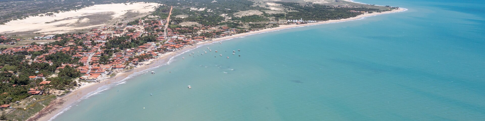 Vista aérea de uma vila costeira com praia, barcos e um mar azul e límpido.