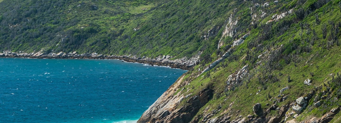 Paisagem costeira com águas azul-turquesa, colinas verdes e falésias rochosas.