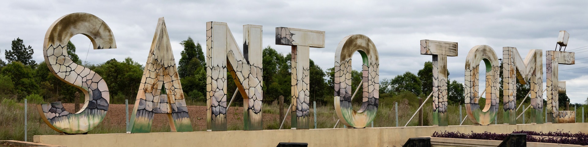 Uma grande escultura ao ar livre com a inscrição 'SANTO TONE', apresentando uma textura de pedra rachada.