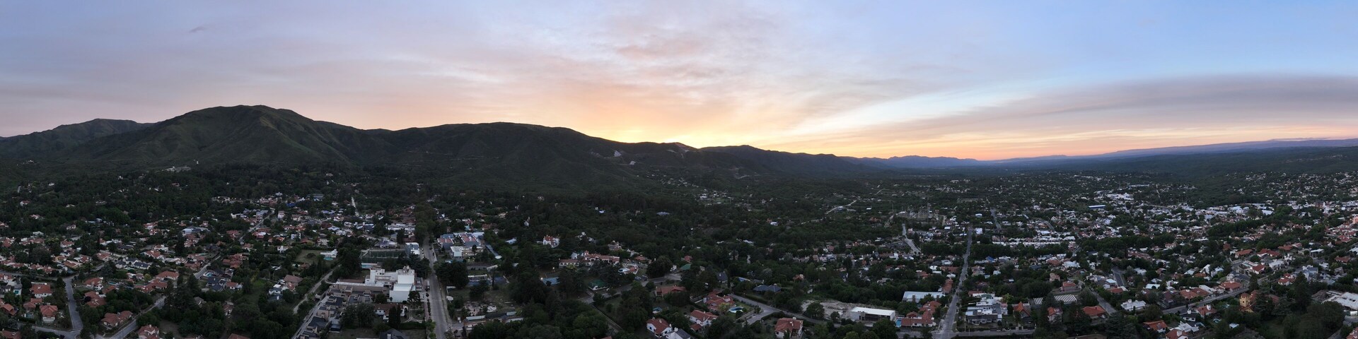Vista aérea de uma cidade com uma montanha ao fundo e um céu ao pôr do sol.