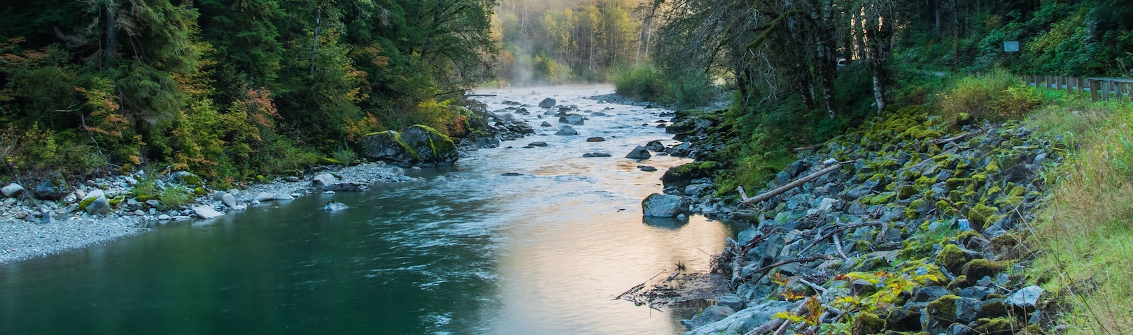 Um rio serpenteando por um vale florestado, com árvores densas e terreno rochoso.
