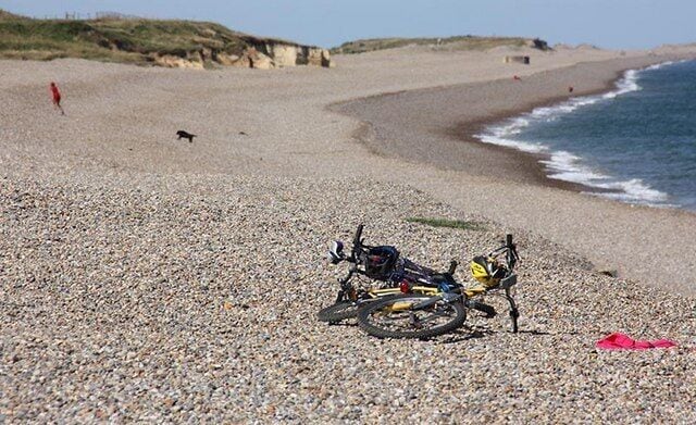 Uma praia de pedras com uma bicicleta e um objeto vermelho na margem.