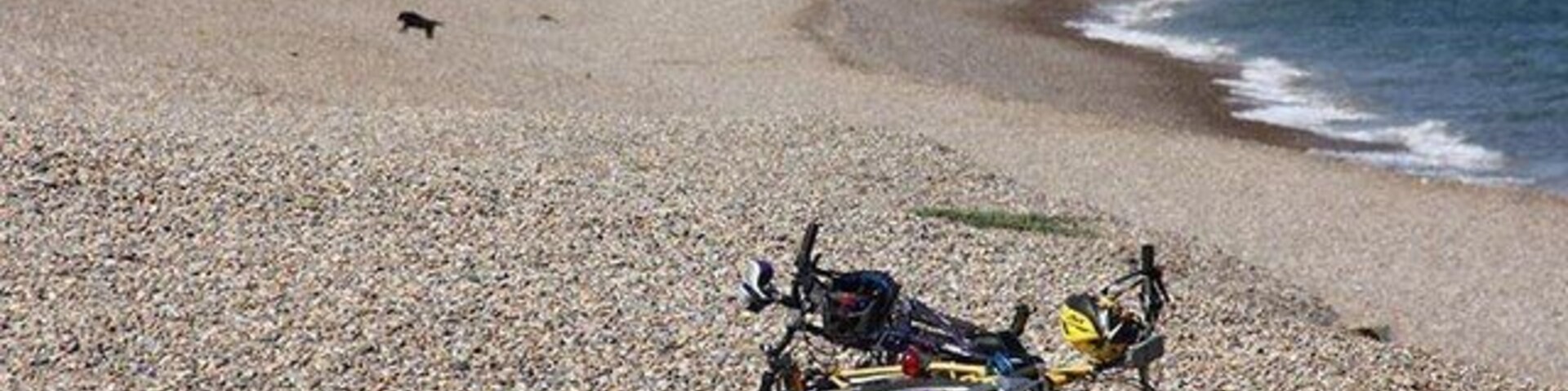 Uma praia de pedras com uma bicicleta e um objeto vermelho na margem.