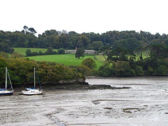 Paisagem costeira com barcos, uma praia arenosa e um campo verde ao fundo.