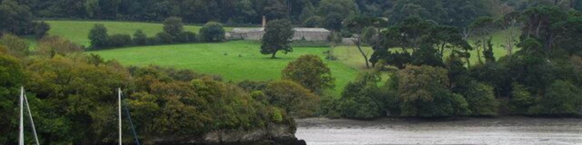 Paisagem costeira com barcos, uma praia arenosa e um campo verde ao fundo.