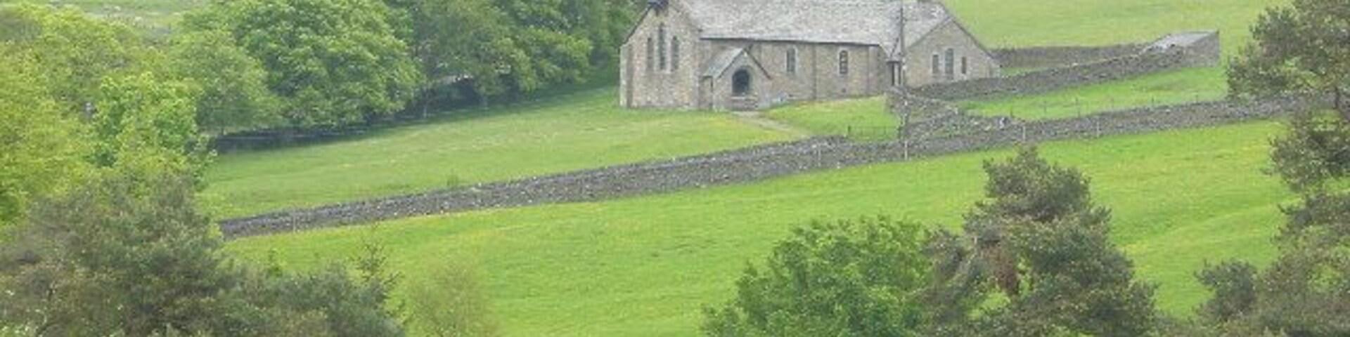 Igreja de pedra rodeada por campos verdes e árvores.
