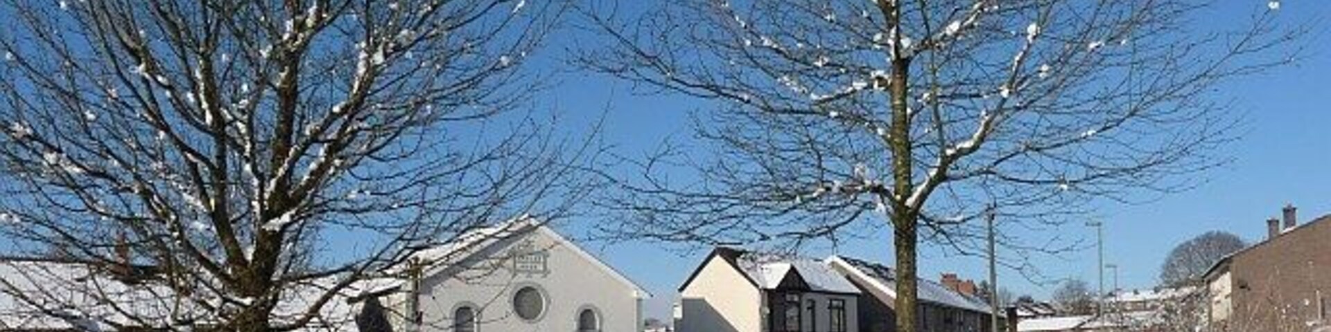 Paisagem coberta de neve com árvores sem folhas e uma igreja.