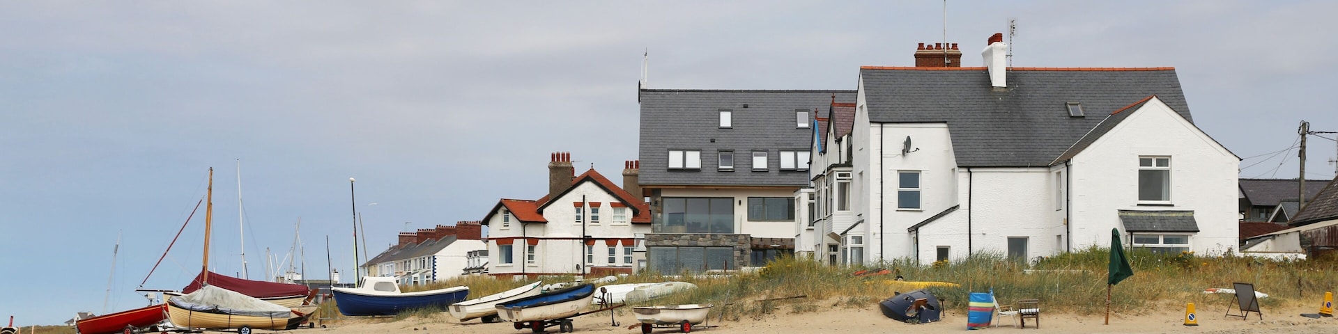 Uma praia arenosa com vários barcos e uma fileira de casas.