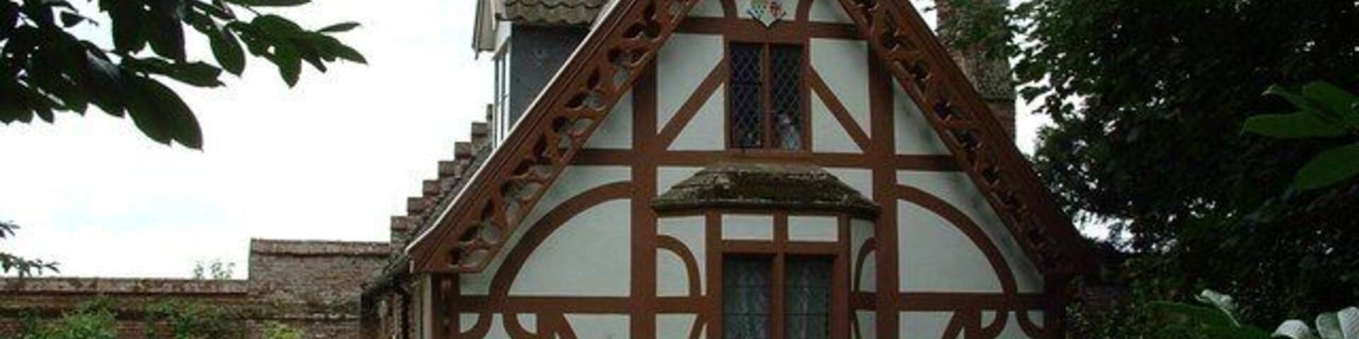 Uma casa em estilo Tudor com telhado íngreme, paredes brancas com vigas de madeira escura e um jardim bem cuidado com diversas plantas e flores.