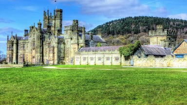 Um castelo grande e histórico, com várias torres e um jardim bem cuidado em primeiro plano.