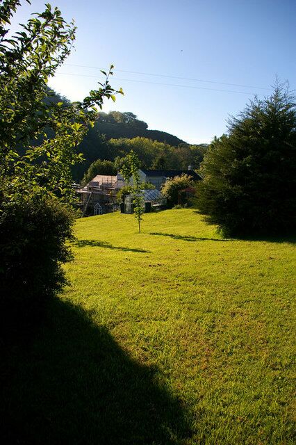 Um campo gramado com uma casa e árvores ao fundo.