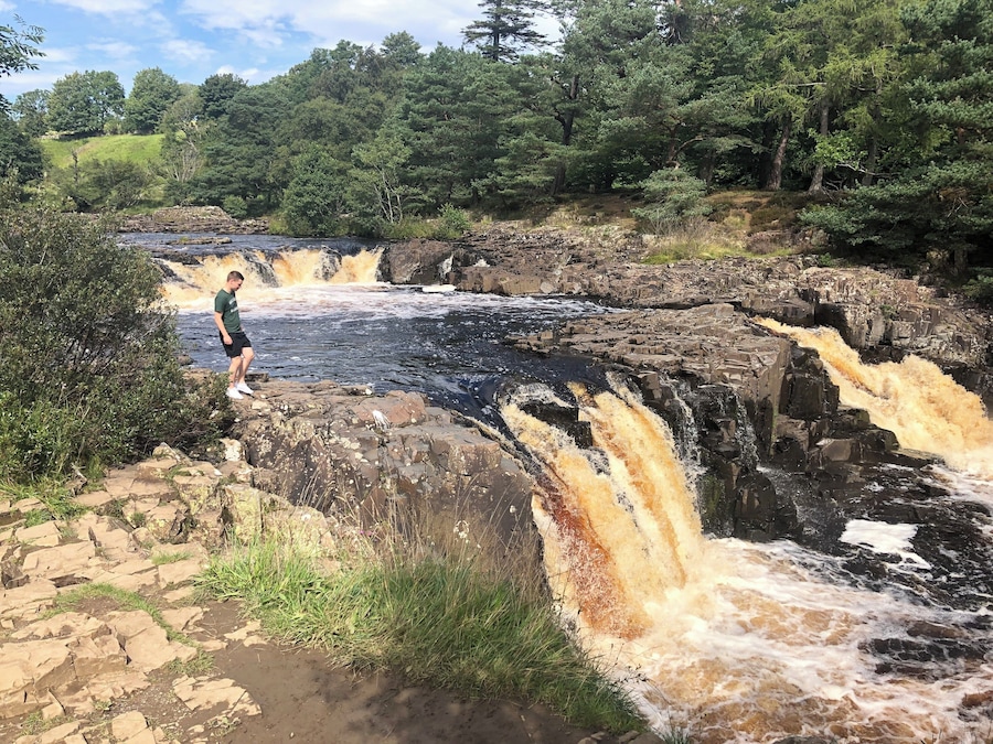 Uma cascata despencando sobre terreno rochoso, cercada por floresta densa.
