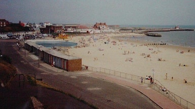 Uma praia com pessoas, uma piscina e edifícios ao fundo.