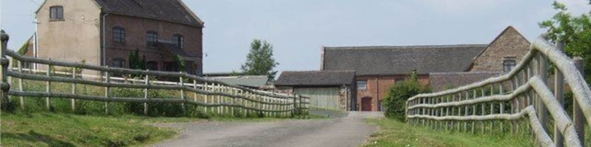 Uma estrada rural que leva a uma casa grande com cerca e um celeiro ao fundo.