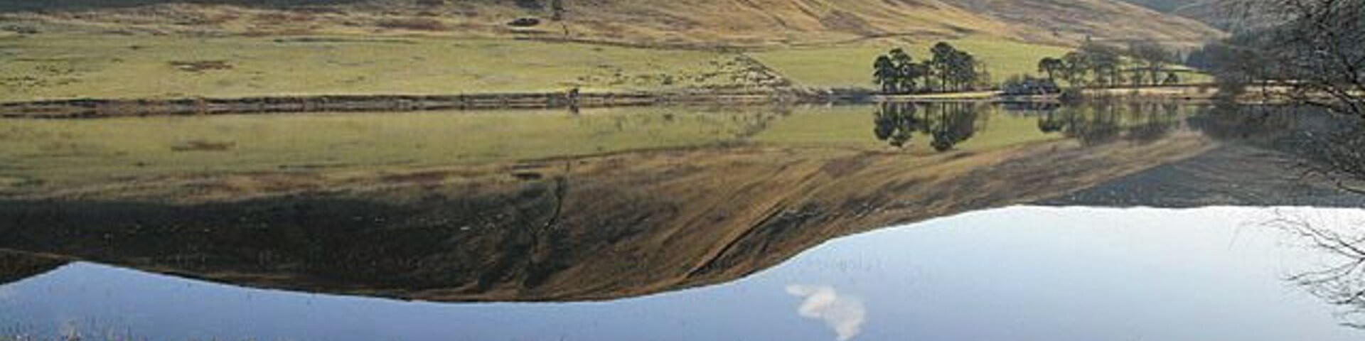 Um lago tranquilo refletindo colinas e um céu claro.