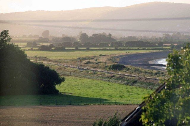 Paisagem rural com campos, um rio e colinas ao longe.