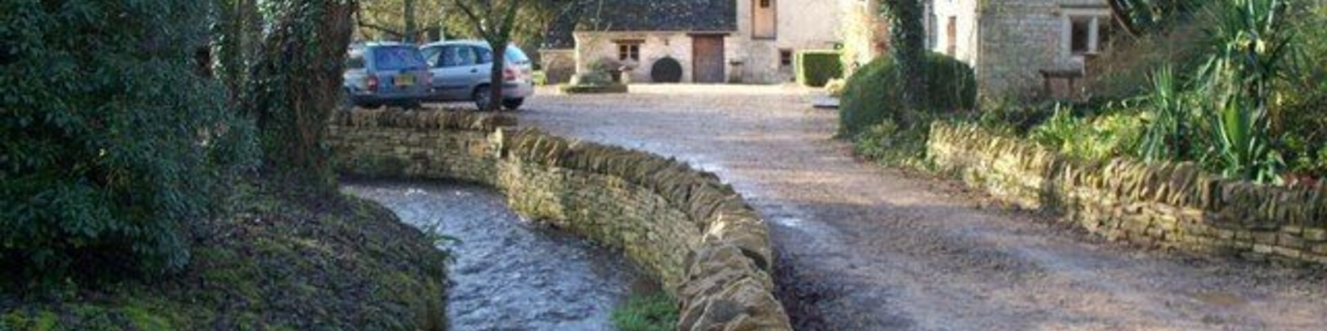 River Coln at Syreford The infant River Coln runs alongside the road in this attractive village. The river has just passed under a bridge which has taken it from one side of the road to the other.