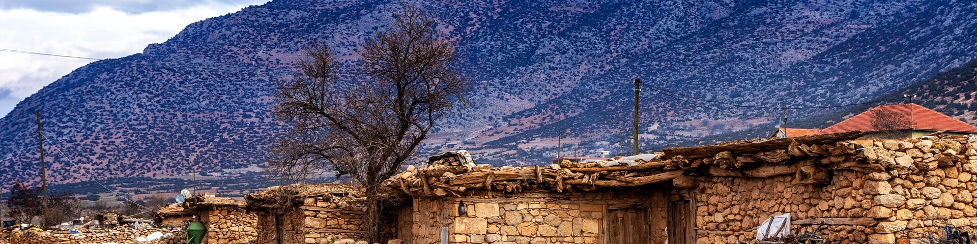 Uma estrada rural com edifícios de pedra e uma montanha ao fundo.