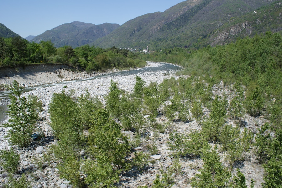 Um rio serpenteia por uma paisagem rochosa, com vegetação verde e montanhas ao fundo.