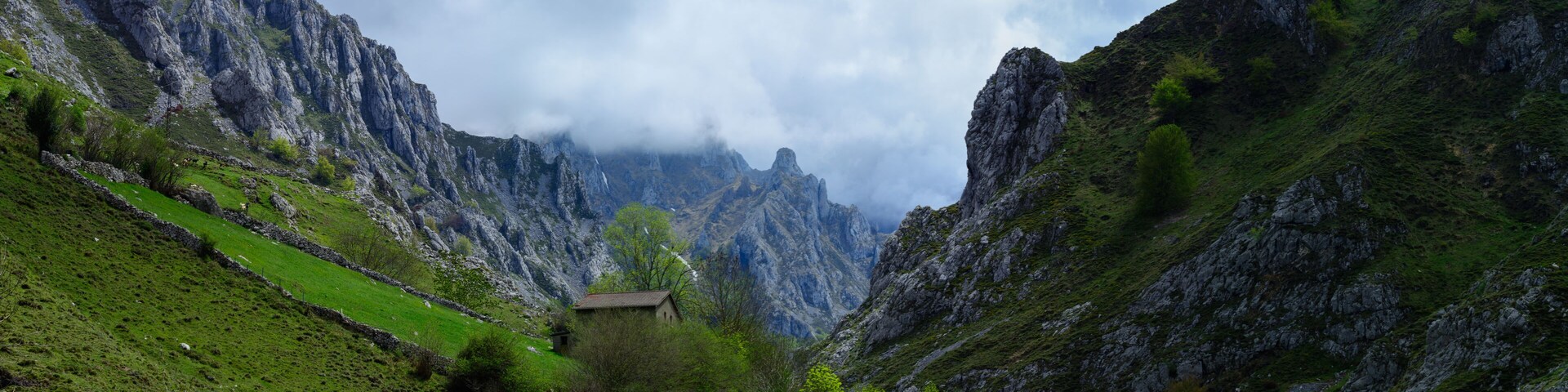 Paisagem montanhosa com uma estrada sinuosa, um pequeno edifício e vegetação verde exuberante.