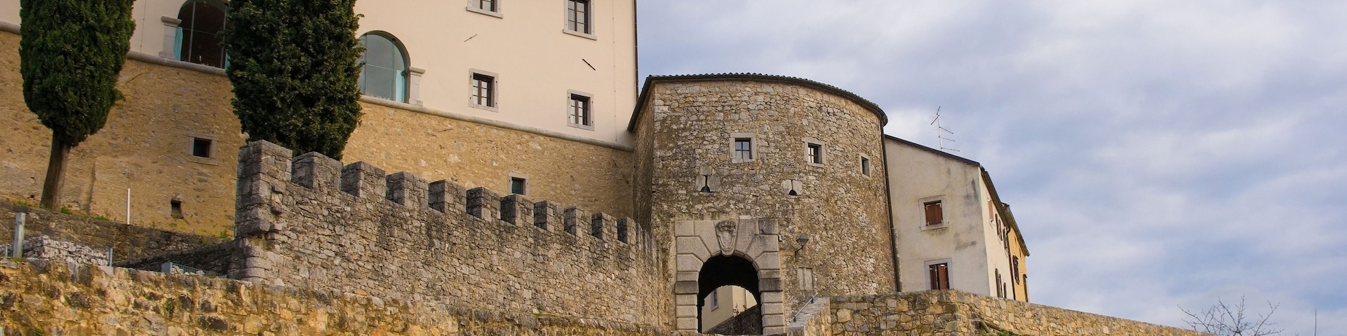 Um edifício histórico de pedra com uma torre redonda, um caminho pavimentado e um muro de pedra.