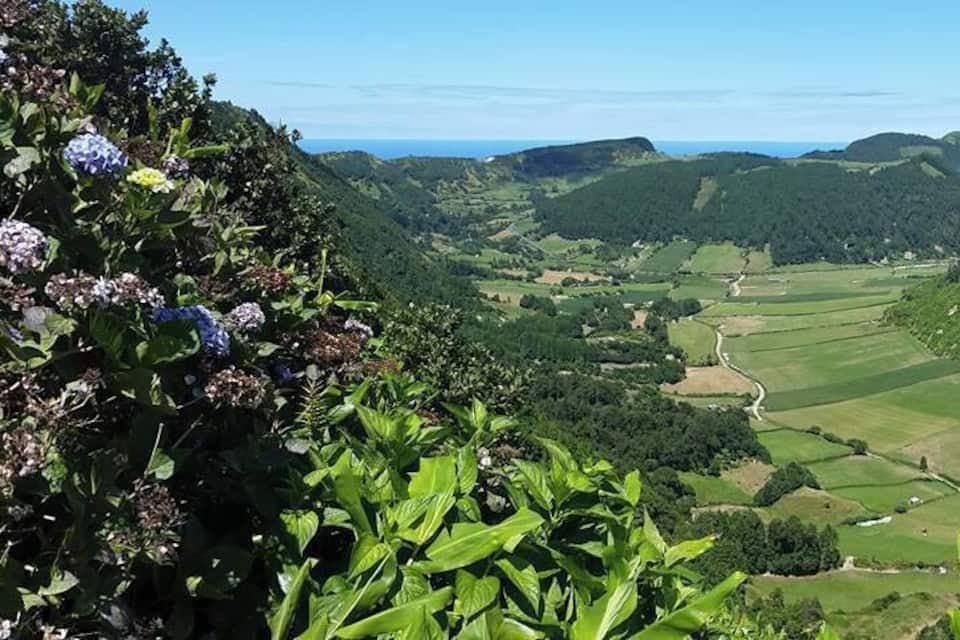 Um vale com campos, um lago e montanhas ao longe.