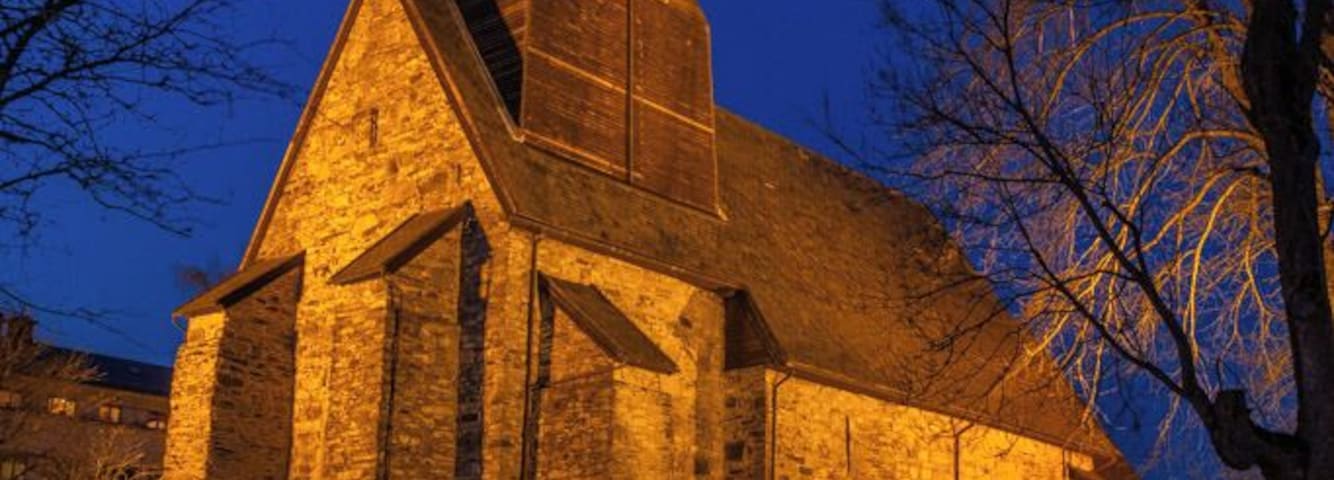 Uma igreja de pedra com um campanário pontiagudo, iluminada por uma luz quente.