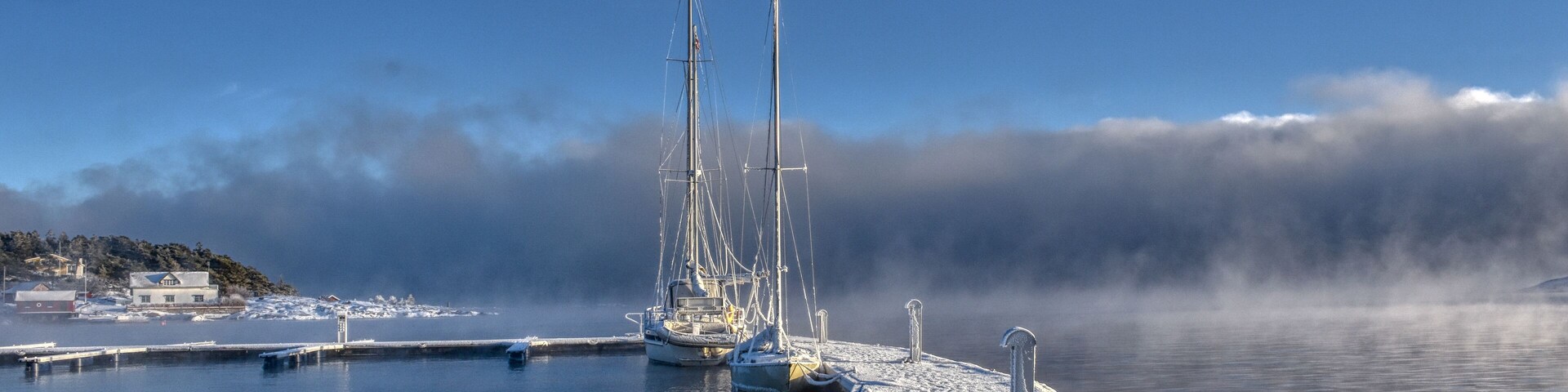 Uma marina com um veleiro atracado, águas calmas e um cais nevado.