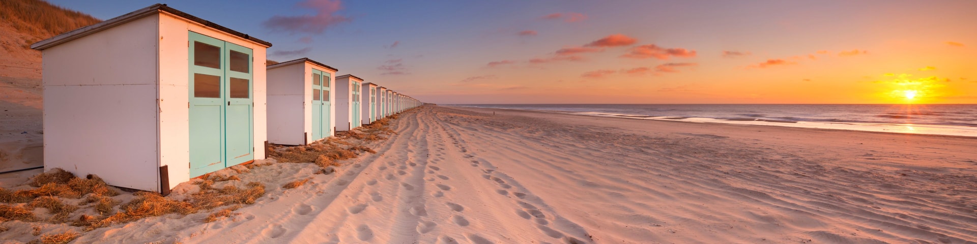 Uma praia com pegadas que levam a uma fileira de cabanas de praia.