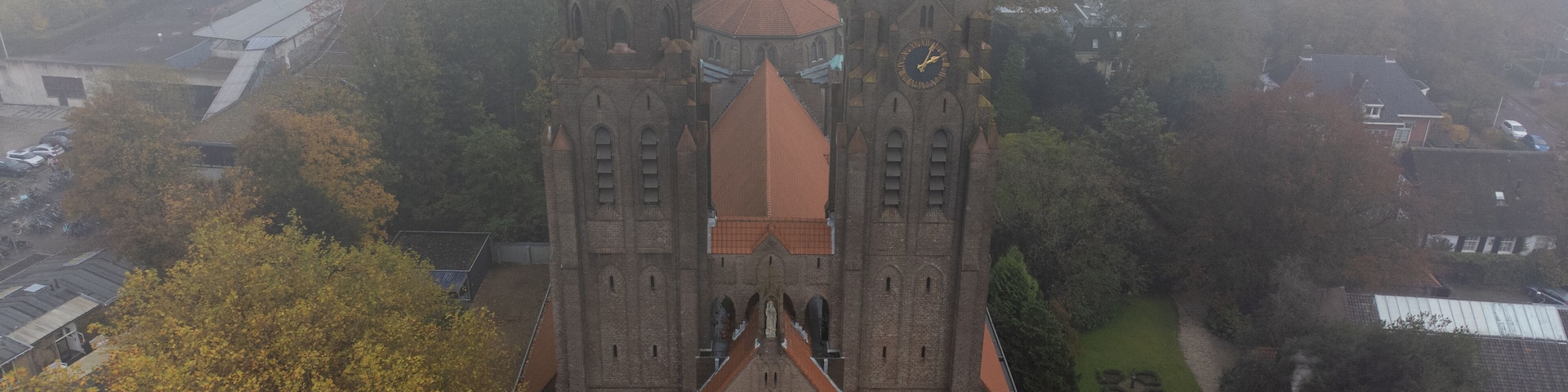 Igreja com duas torres e uma torre central, rodeada por árvores de outono e uma paisagem nevoenta.