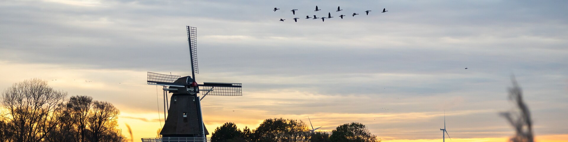 Um moinho de vento à beira da água ao pôr do sol.