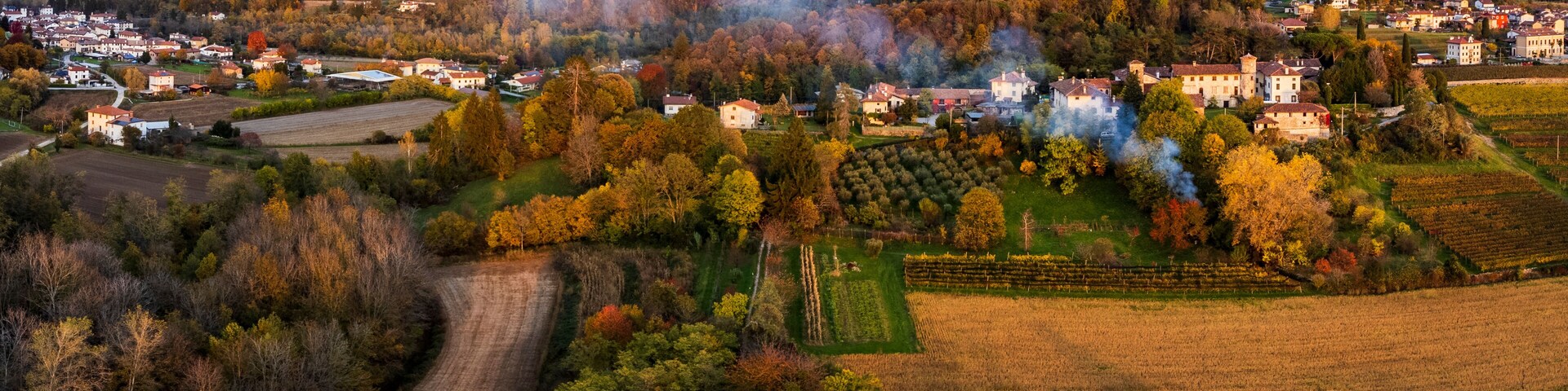 Paisagem rural com uma aldeia, campos e montanhas ao fundo.